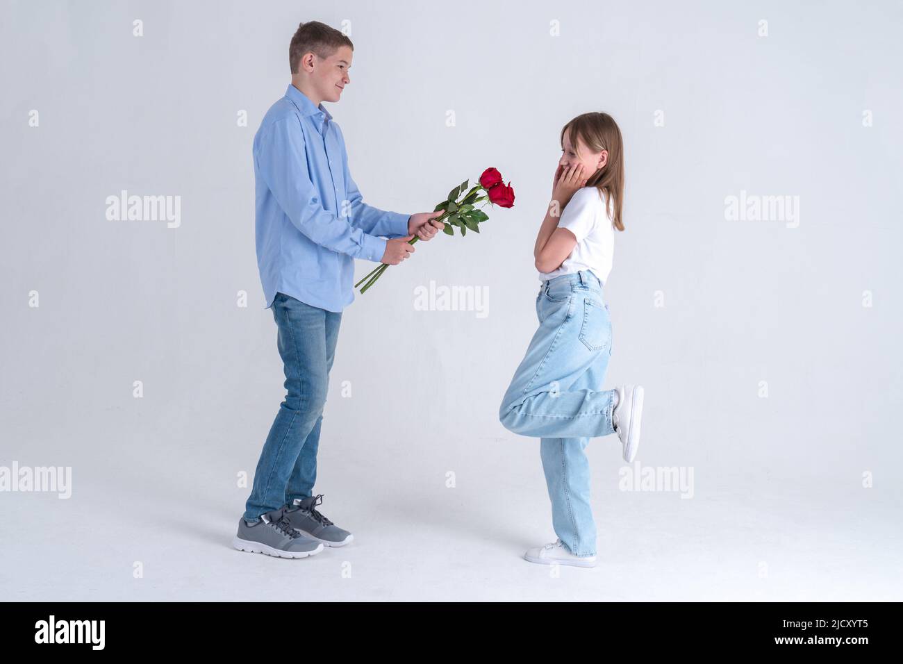 Teen boy gives his girlfriend a bouquet of red roses on a white ...