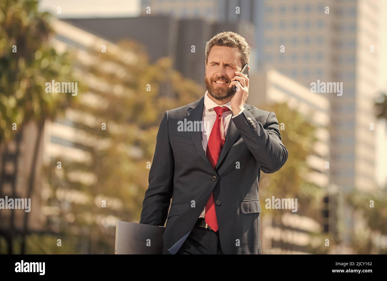 cheerful successful businessman in suit talking on phone standing ...