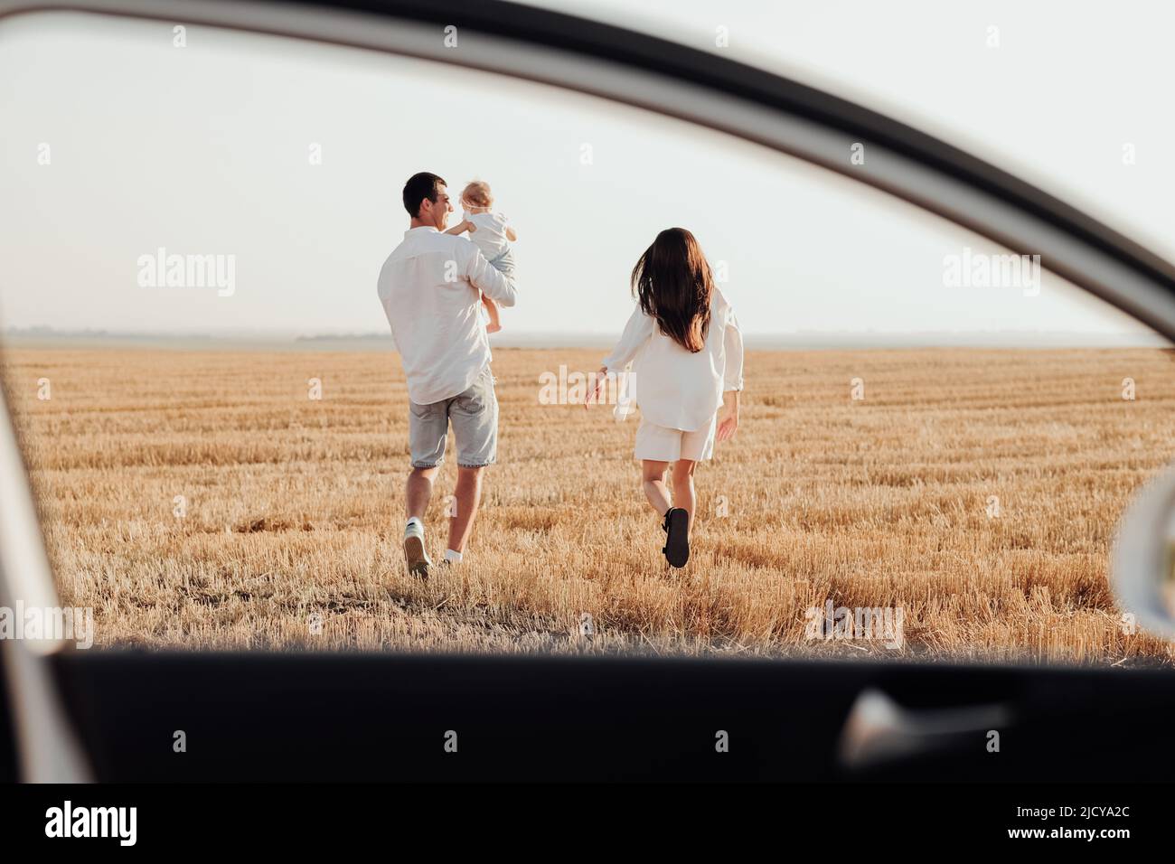 Young Family Walking in the Field at Sunset, Back View Through Car ...