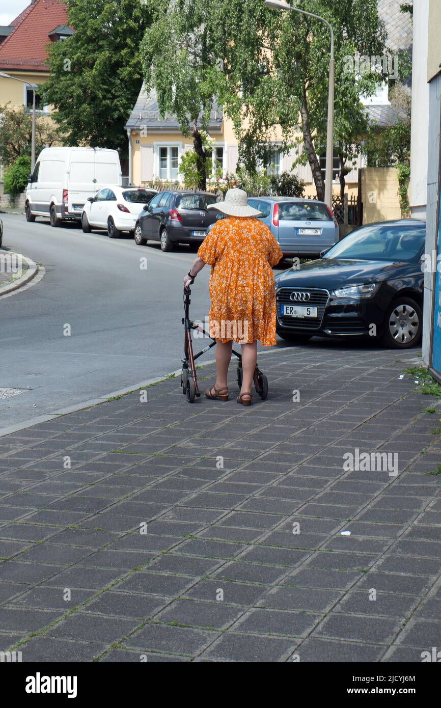 Woman passerby in flowered dress and with white hat crossing a street ...