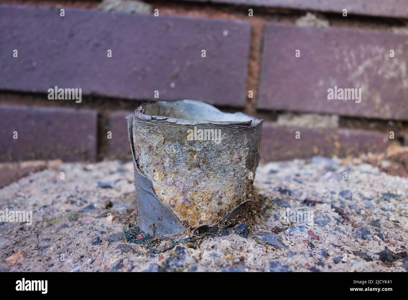 broken and rusted steel post in the pavement with a brick wall in the ...