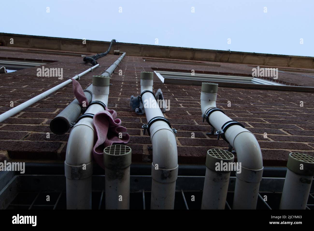 looking up at three plastic pipes on the side of a building with vents ...