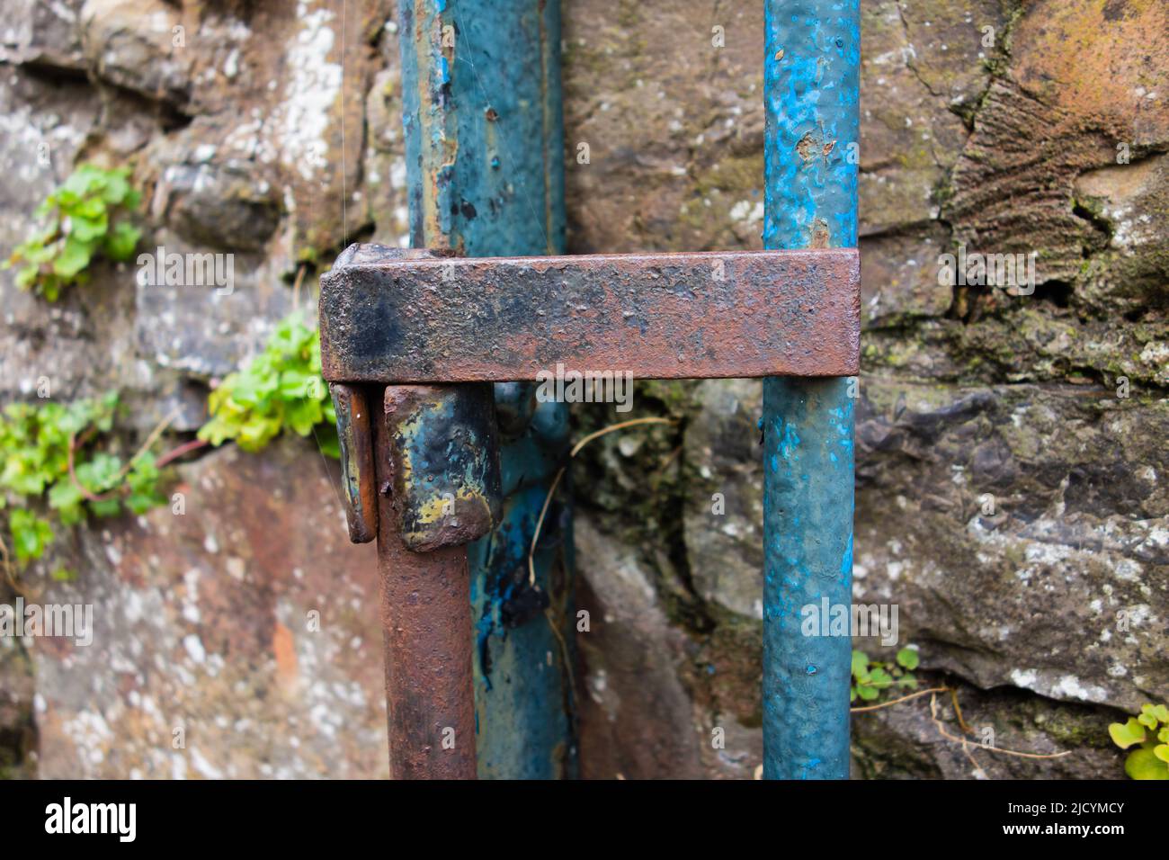 old blue iron gate and hinge and a old stone wall in the background ...