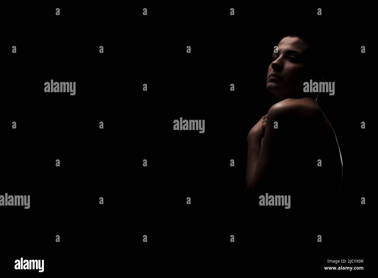 Portrait of a girl with short hair against dark background. Side lit ...