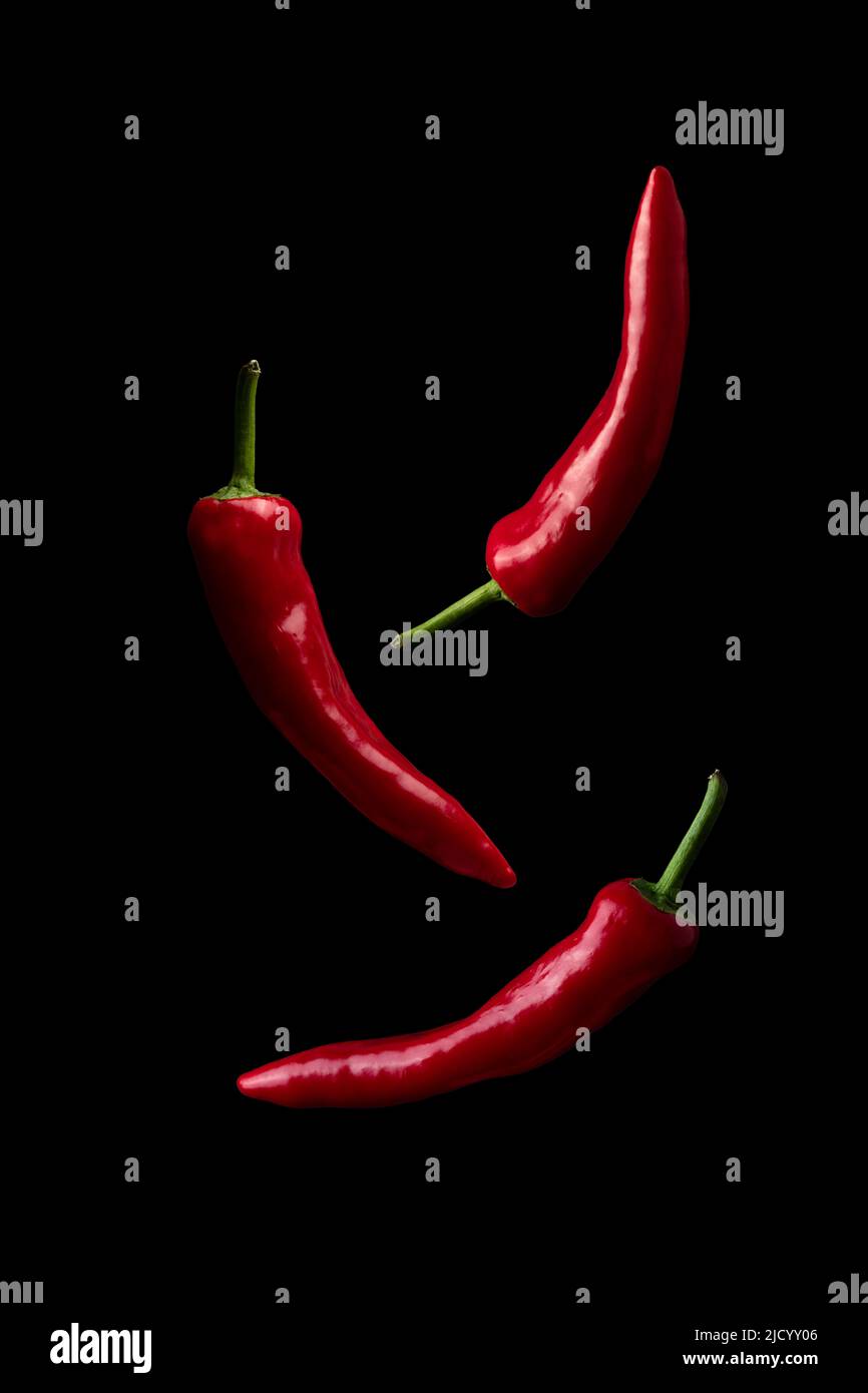 Three red peppers are falling on black background Stock Photo - Alamy
