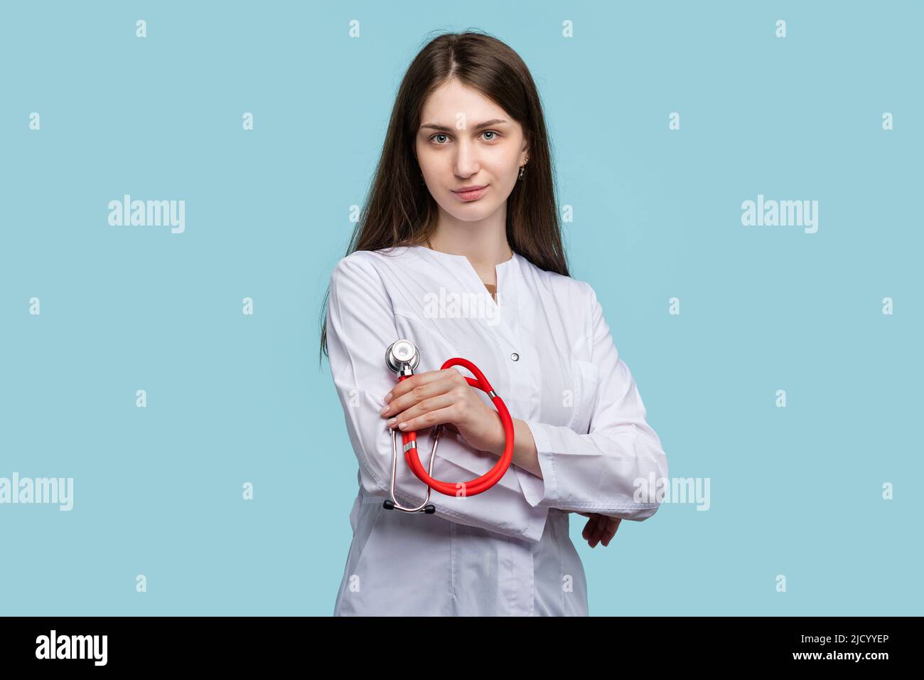Female Intern Doctor posing with arms crossed looking at camera on blue ...