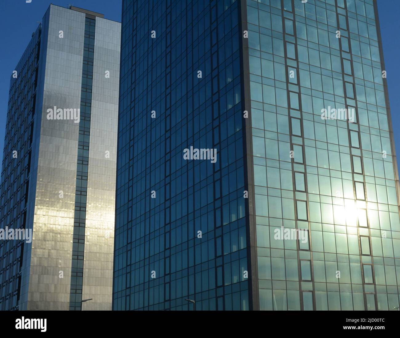 two modern architecture buildings with a sun reflecting on windows and ...
