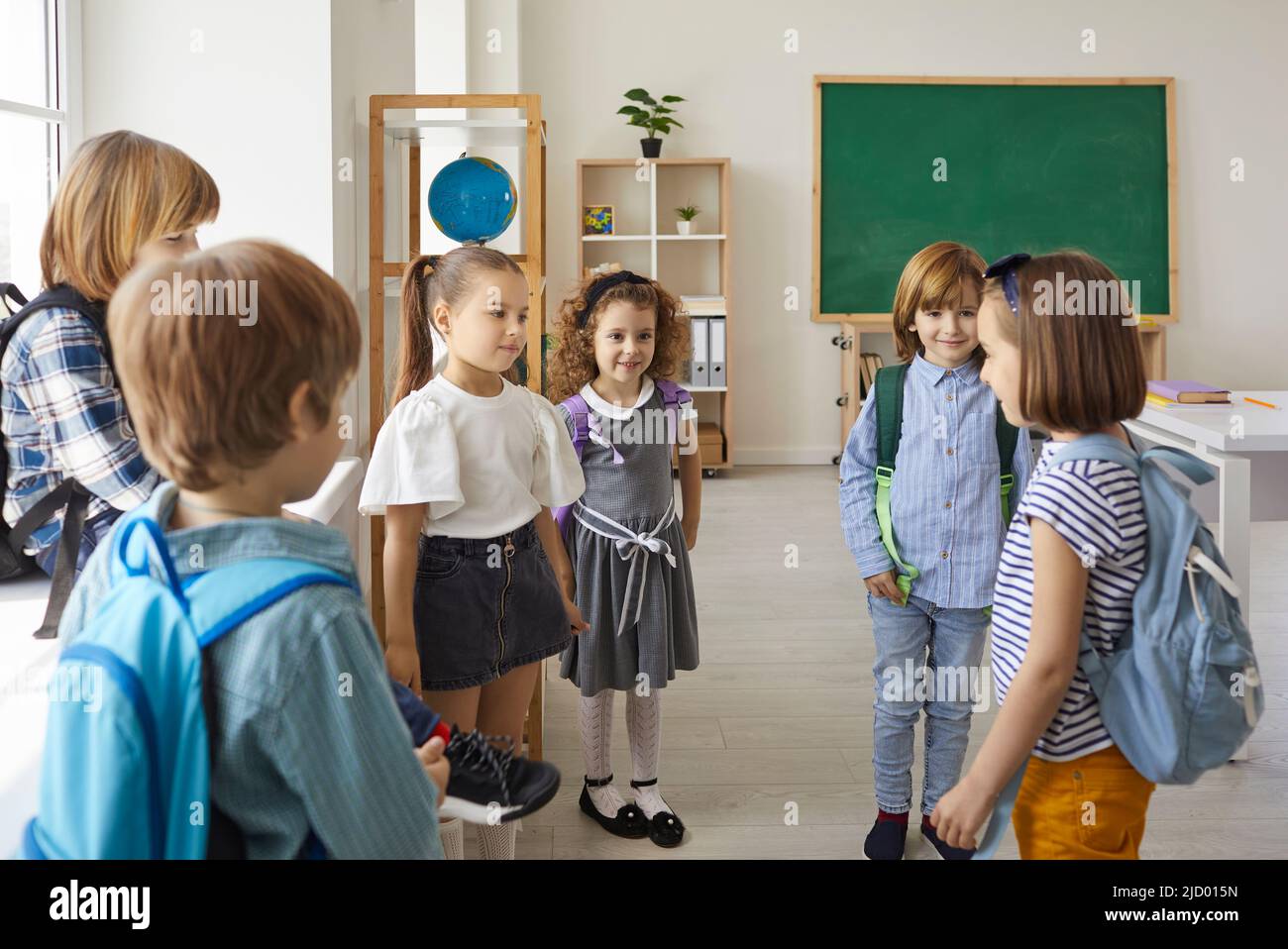 Happy little school children standing in the classroom and talking to ...
