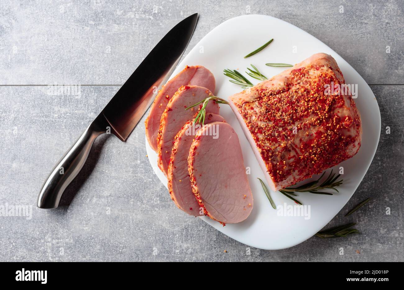 Spicy smoked ham with rosemary and kitchen knife on a grey stone table ...