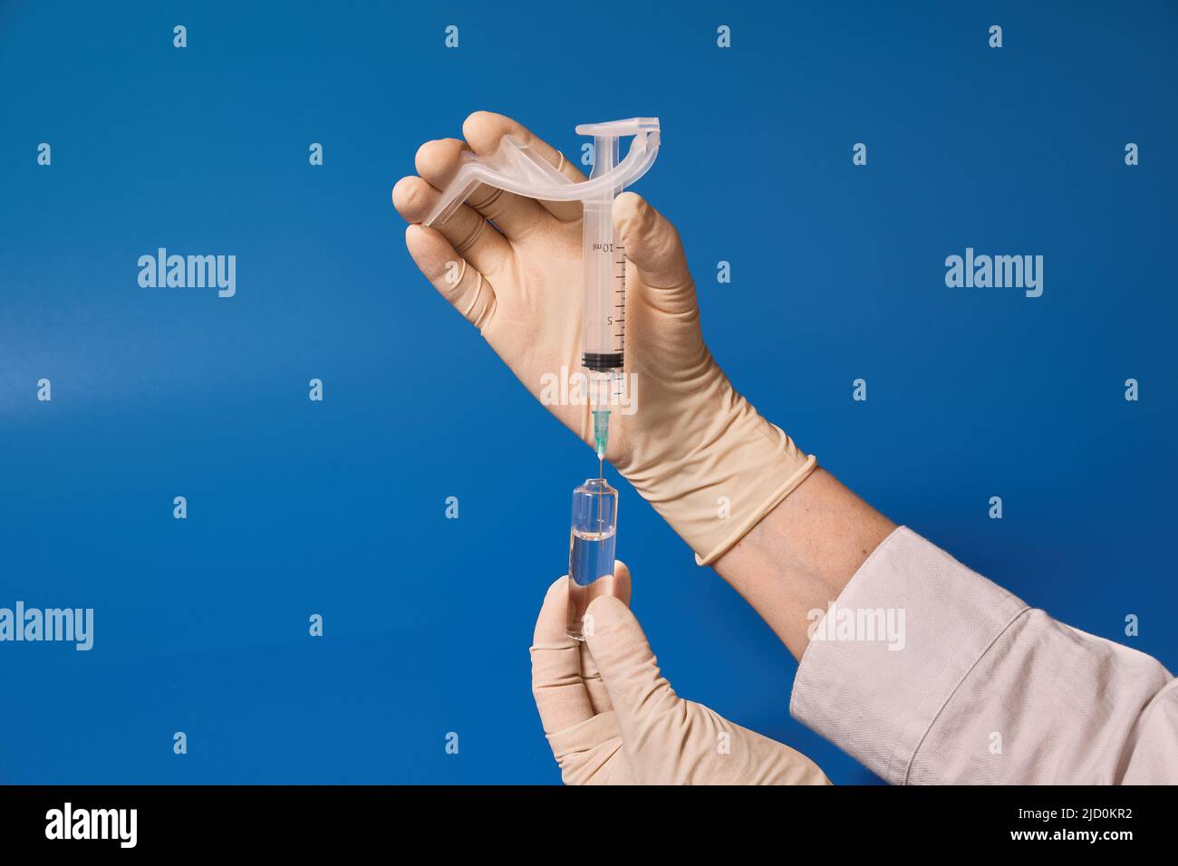 Gloved hand holding syringe on blue background Stock Photo - Alamy