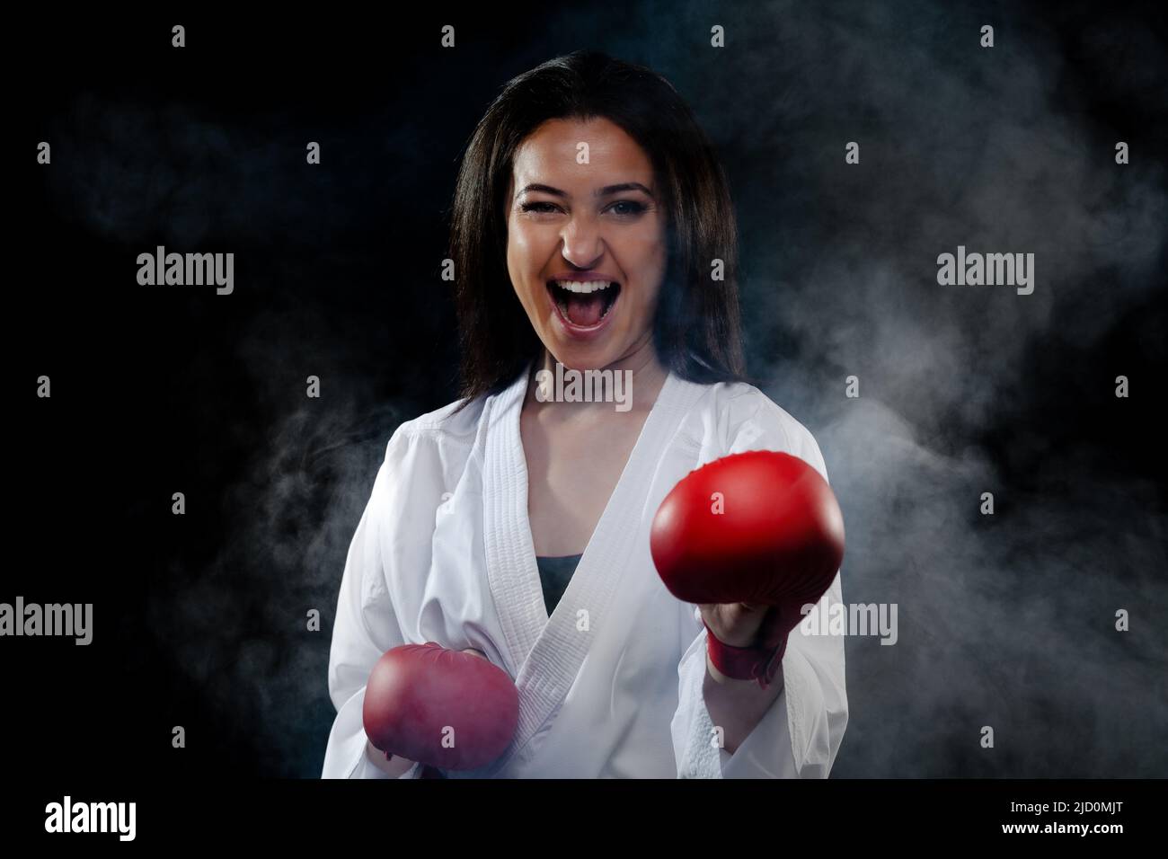 beautiful girl exercising karate pose amnd screaming against fog ...