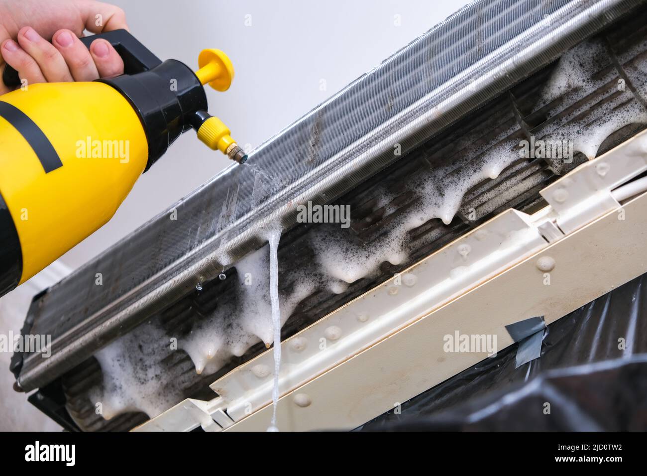 A man washes off a special foam for cleaning air conditioners with a ...
