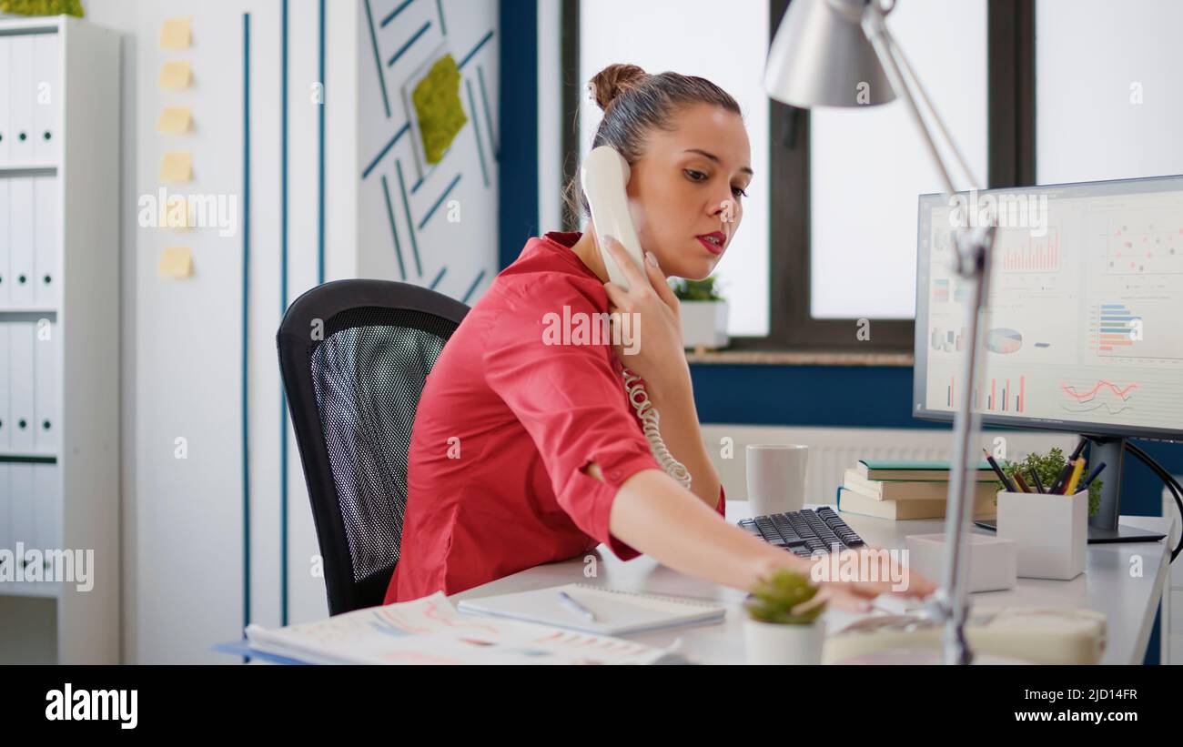 Female secretary using landline phone to take call from manager ...