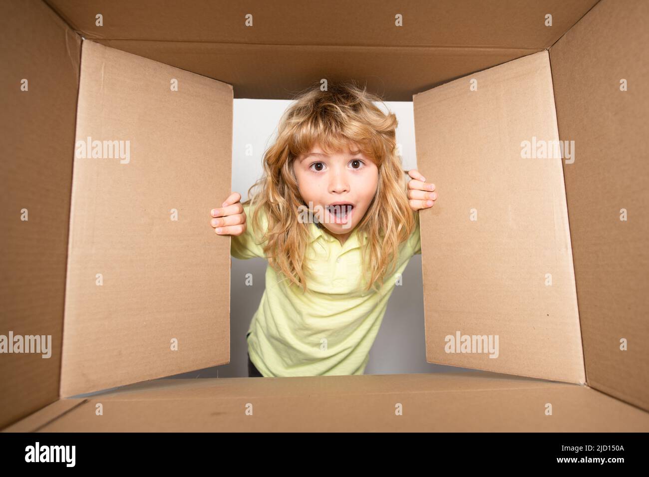 Happy little child boy is opening gift and looking inside cardboard box ...