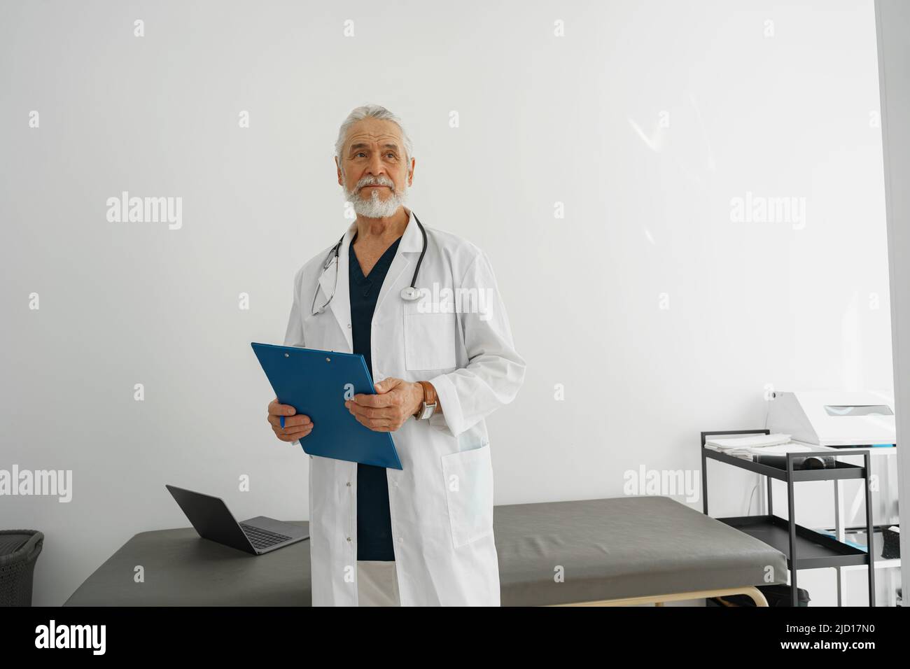 Senior doctor with clipboard standing on her work place in clinic ...