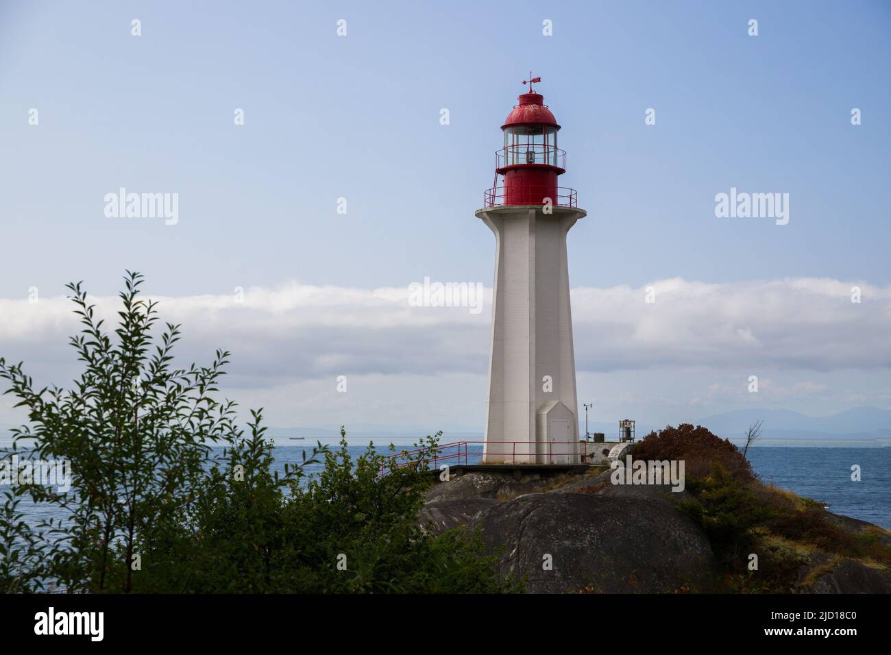 Old Lighthouse in a daytime. Cloudy sky, ocean, rocks and small trees ...
