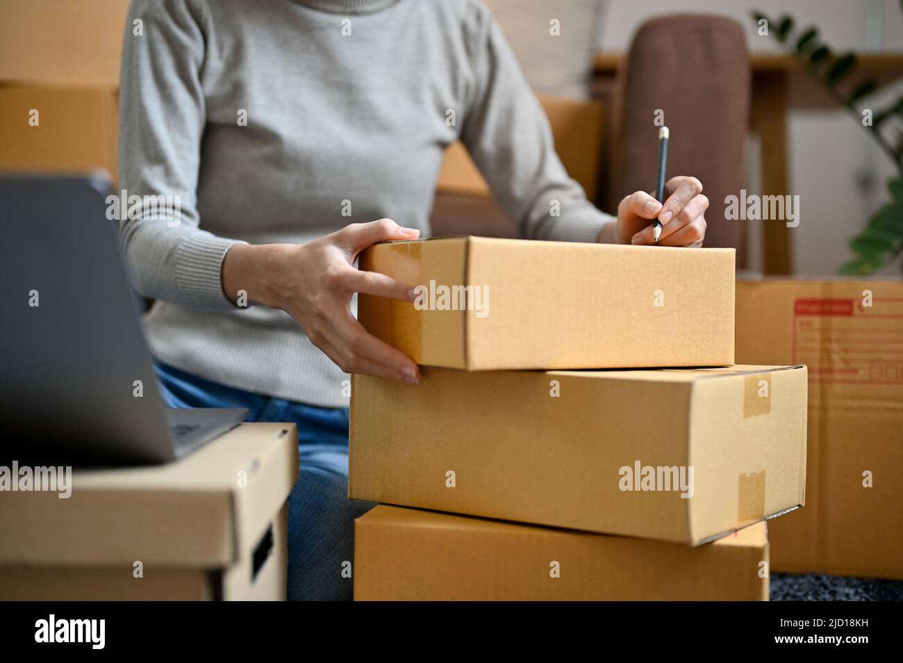 Female online shopping store owner packing a delivery box, writing a ...