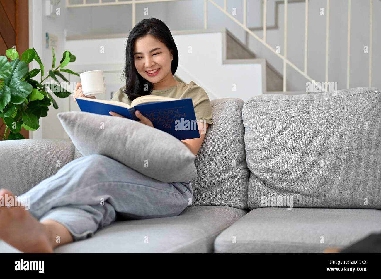 Attractive young asian woman reading a novel book or textbook on her ...