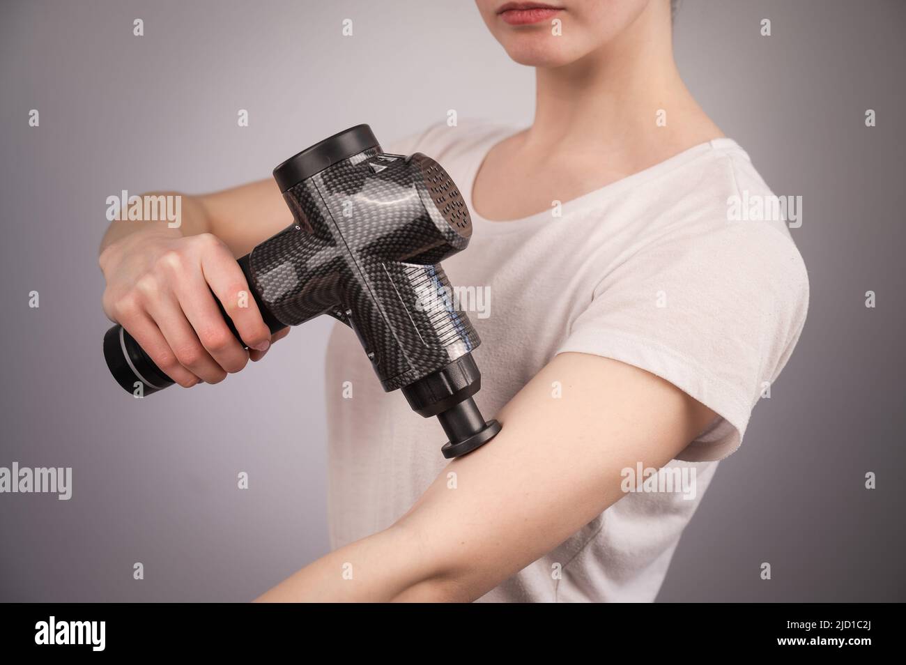 Caucasian woman uses a massager gun for pain in the muscles of the arm ...