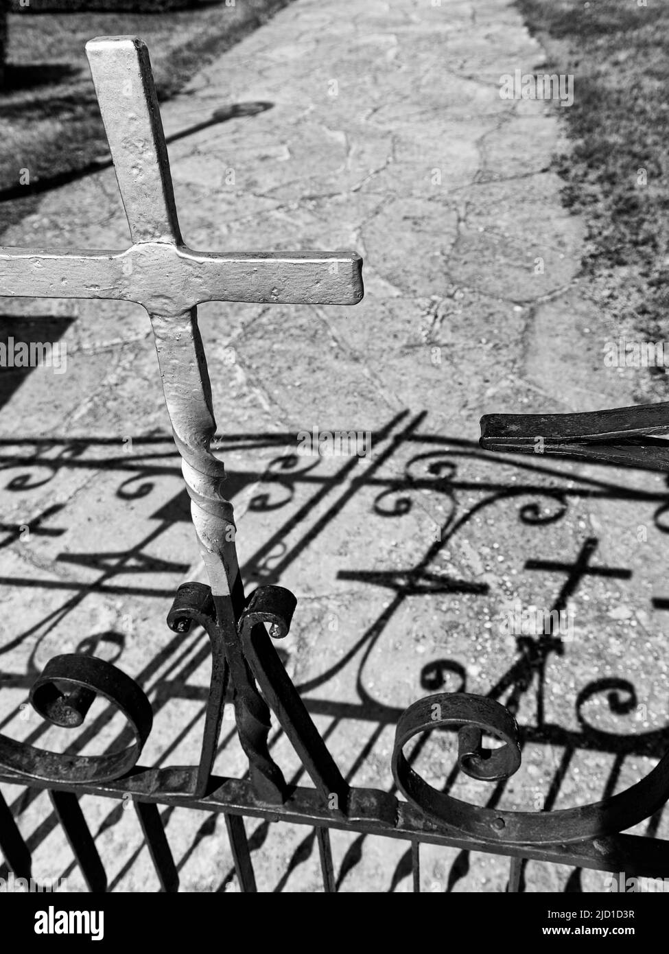 Wrought iron gate with metal cross casting shadows on a path, black and ...