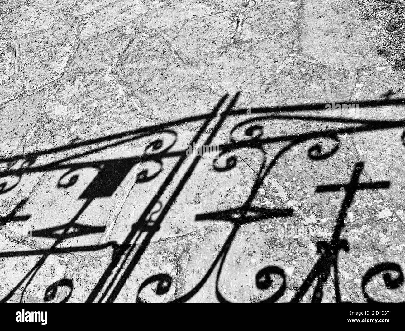 Wrought iron gate with cross casting shadows on a path, black and white ...