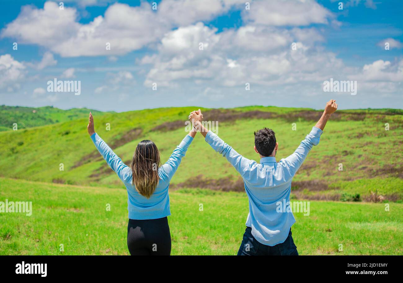 Back view of Happy couple in the field raising hands to the sky ...