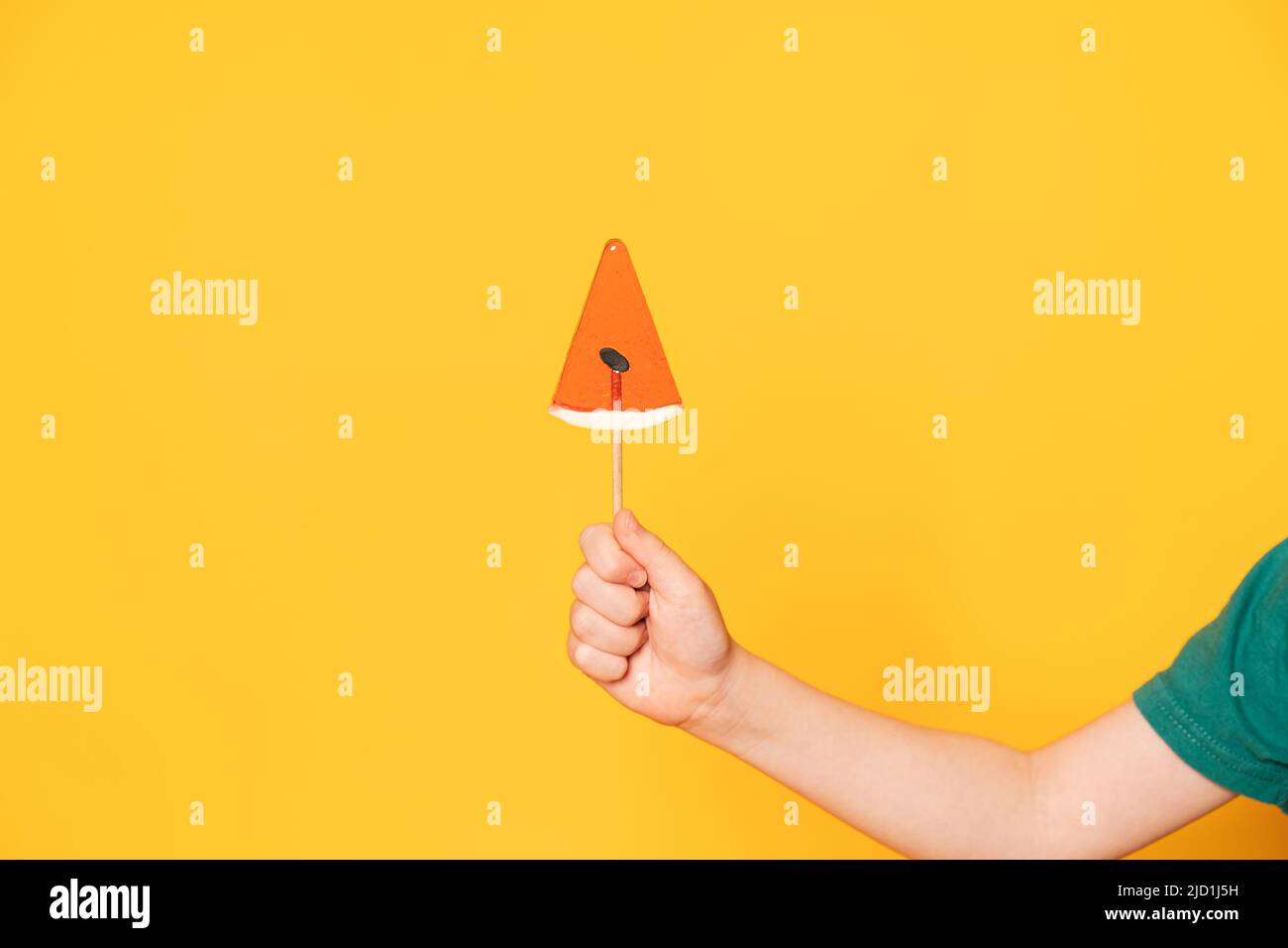 Child's hand holding lollipop in the shape of piece of watermelon ...