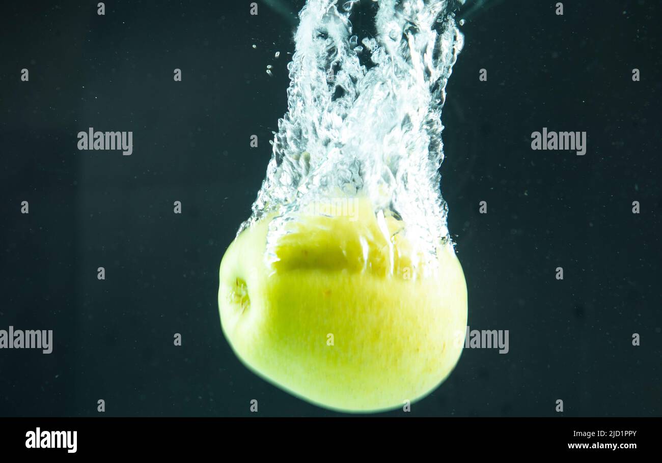 drop green apple in the tank. water is splashed on the black background ...
