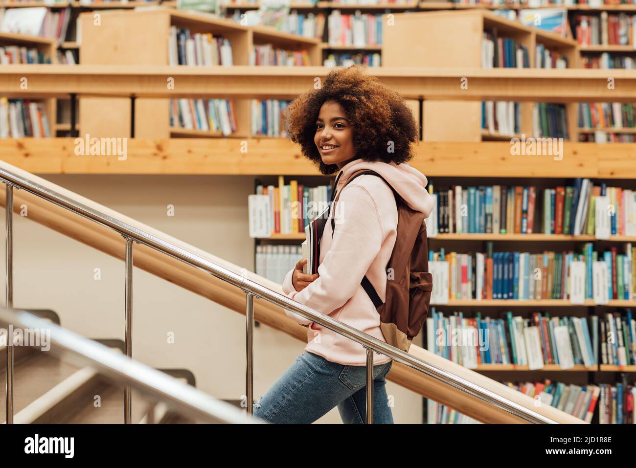 Smiling girl walking on stairs in library. Student in college library ...
