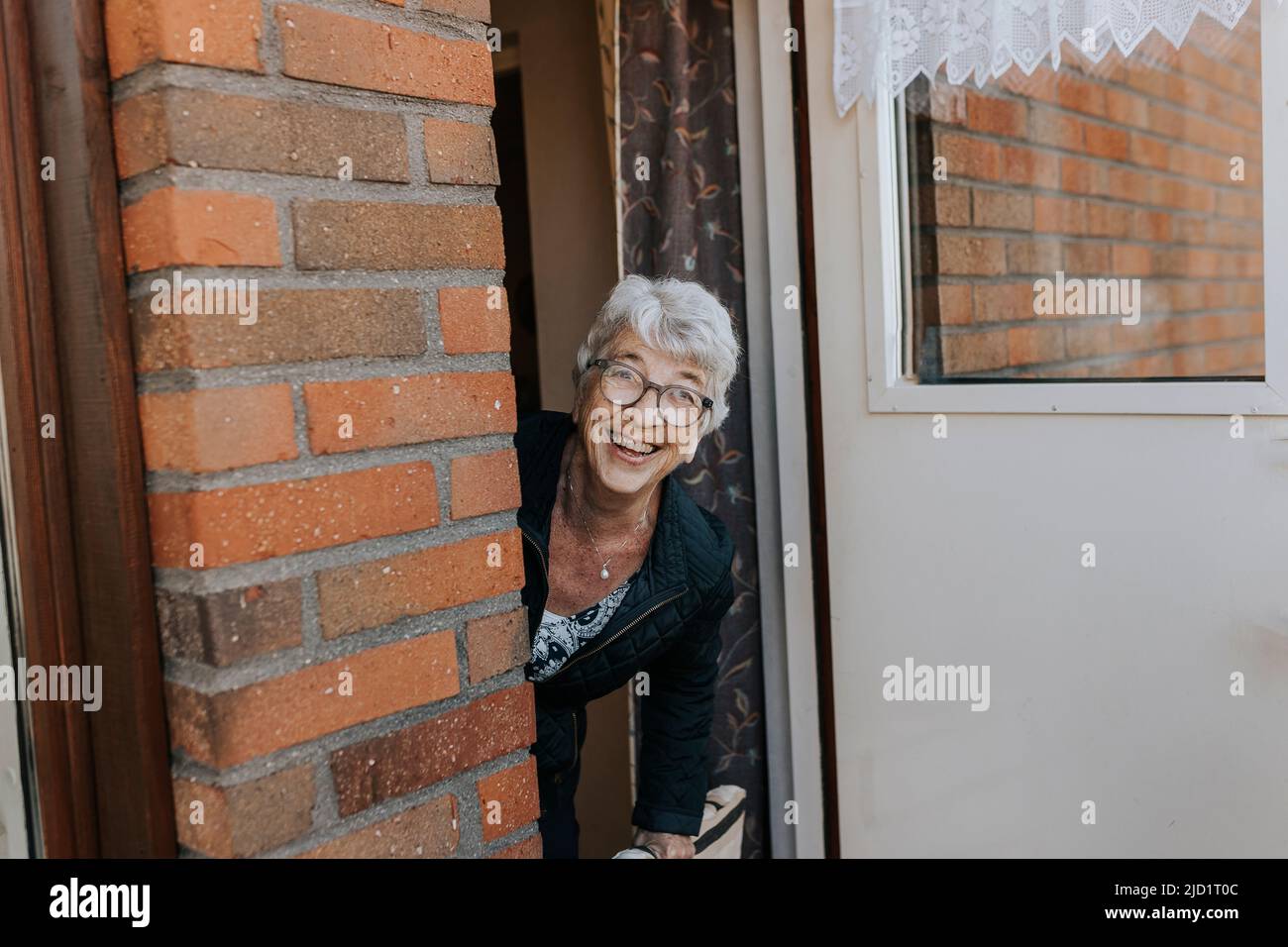 Senior woman looking through open door Stock Photo - Alamy