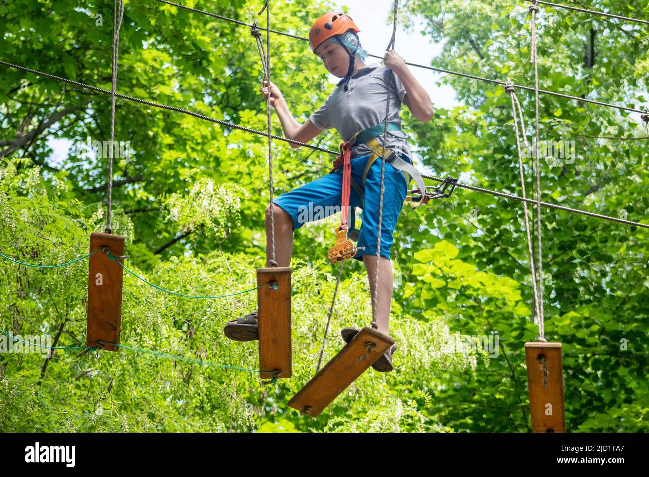 Rope park. A boy teenager in a helmet walks on suspended rope ladders ...