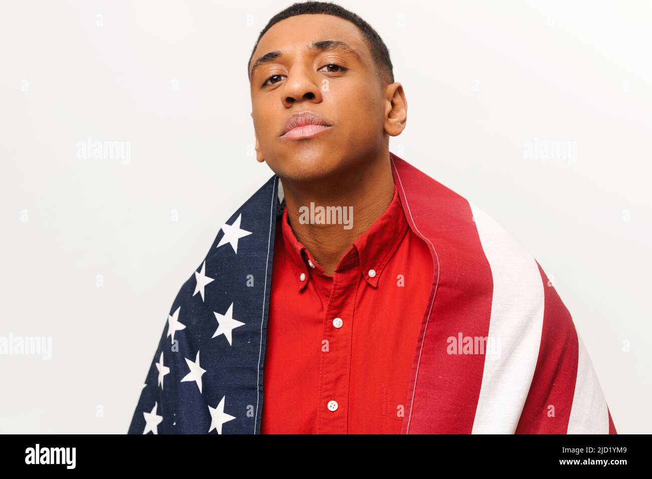 Serious proud African-American guy stands covered with american flag ...