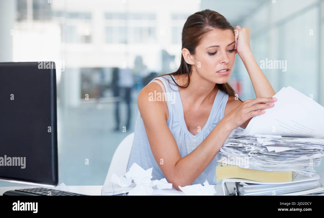 Buried under paperwork. Shot of a stressed out young businesswoman ...