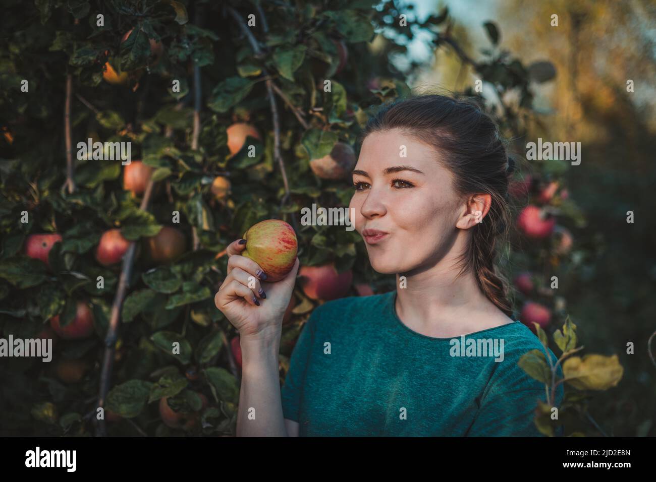 Young woman biting a red apple in the garden and enjoying the flavor of ...
