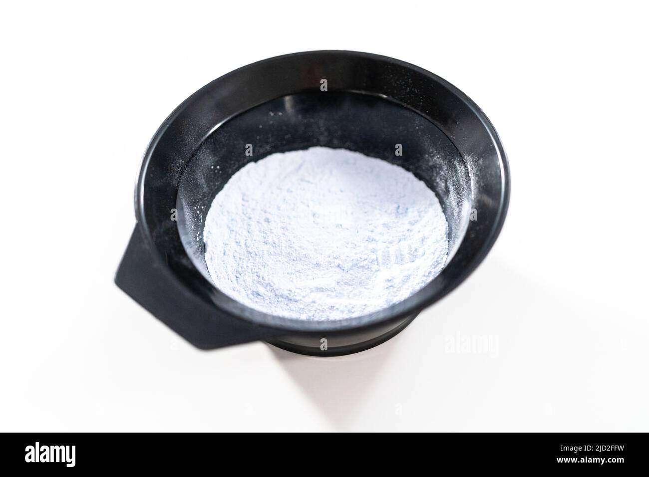 Hair color dye powder in a black plastic mixing bowl on a white ...