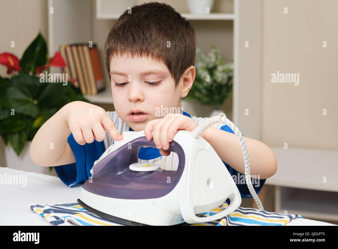 A boy of 4 years learns to hold an iron, iron clothes on an ironing ...