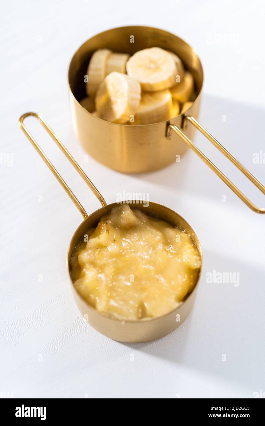 Mashed overripe bananas and sliced riped bananas in metal measuring ...