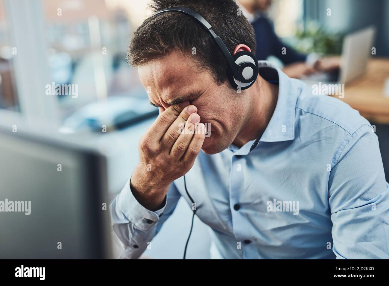 Its been a long workday. Shot of a young call centre agent looking ...