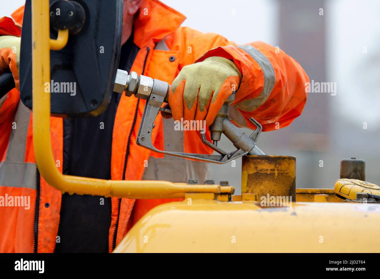 Construction worker in safety gloovs filling excavator with diesel fuel ...