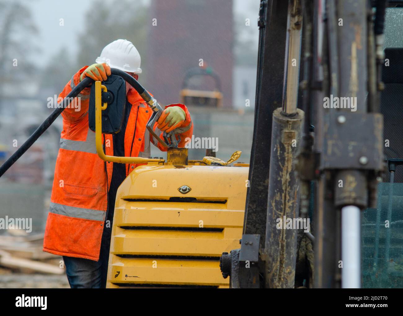 Construction worker in safety gloovs filling excavator with diesel fuel ...