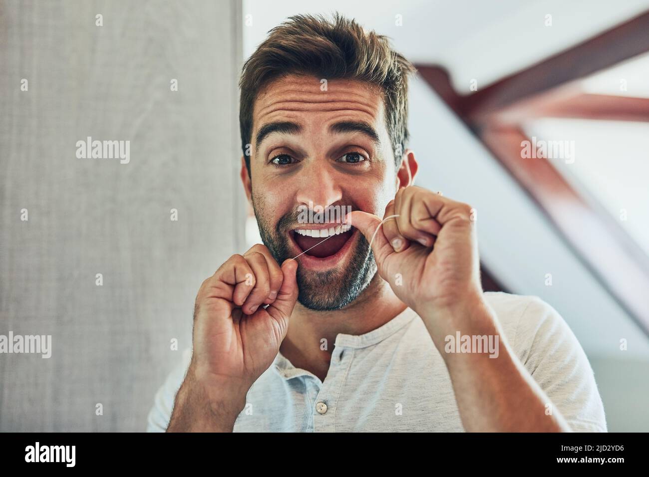 My teeth makes a great smile. Portrait of a cheerful young man flossing his teeth while looking ...