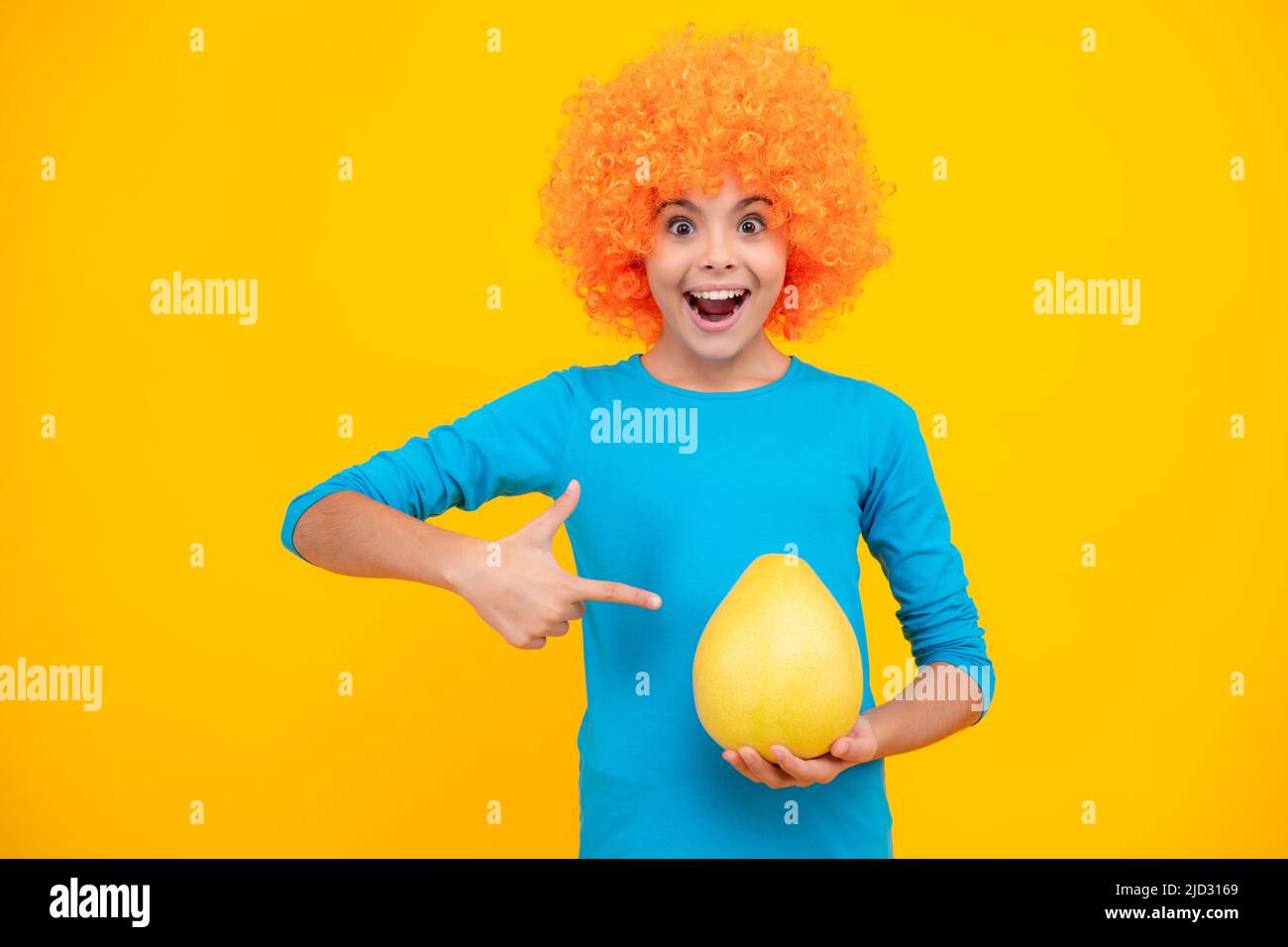 Funny child girl in wig hold big citrus fruit pummelo or pomelo full of ...