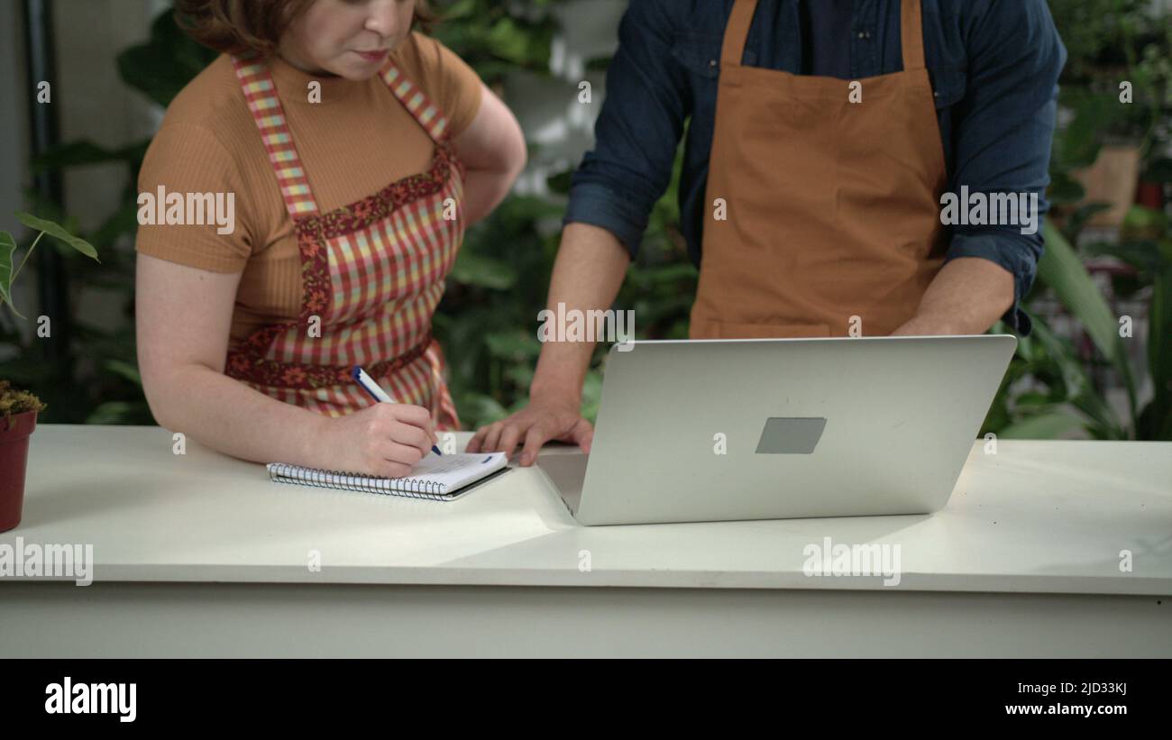 Male and female staff wearing aprons discussing online orders in front ...