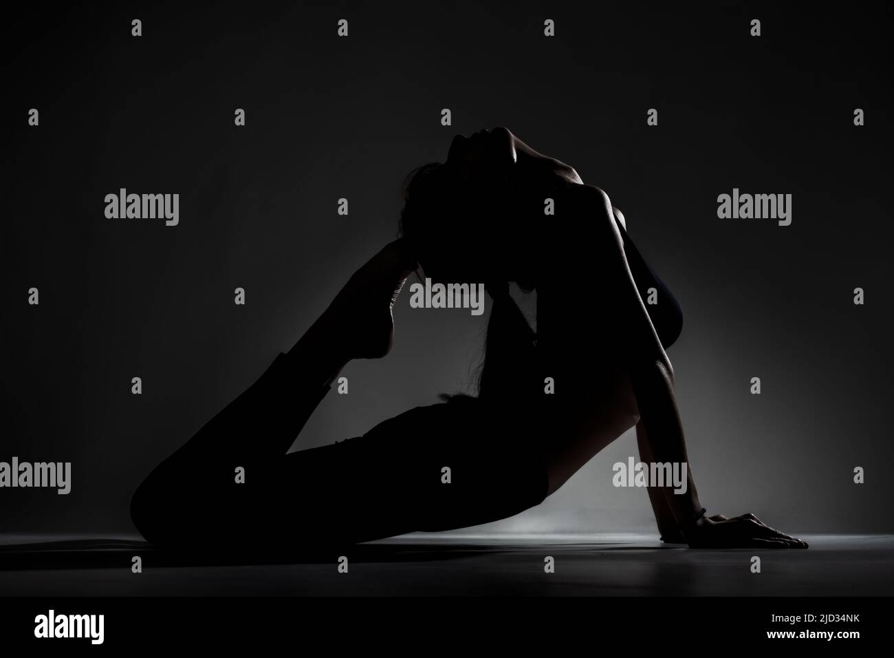 Fit ballerina girl lying and stretching practicing yoga poses. Side lit ...