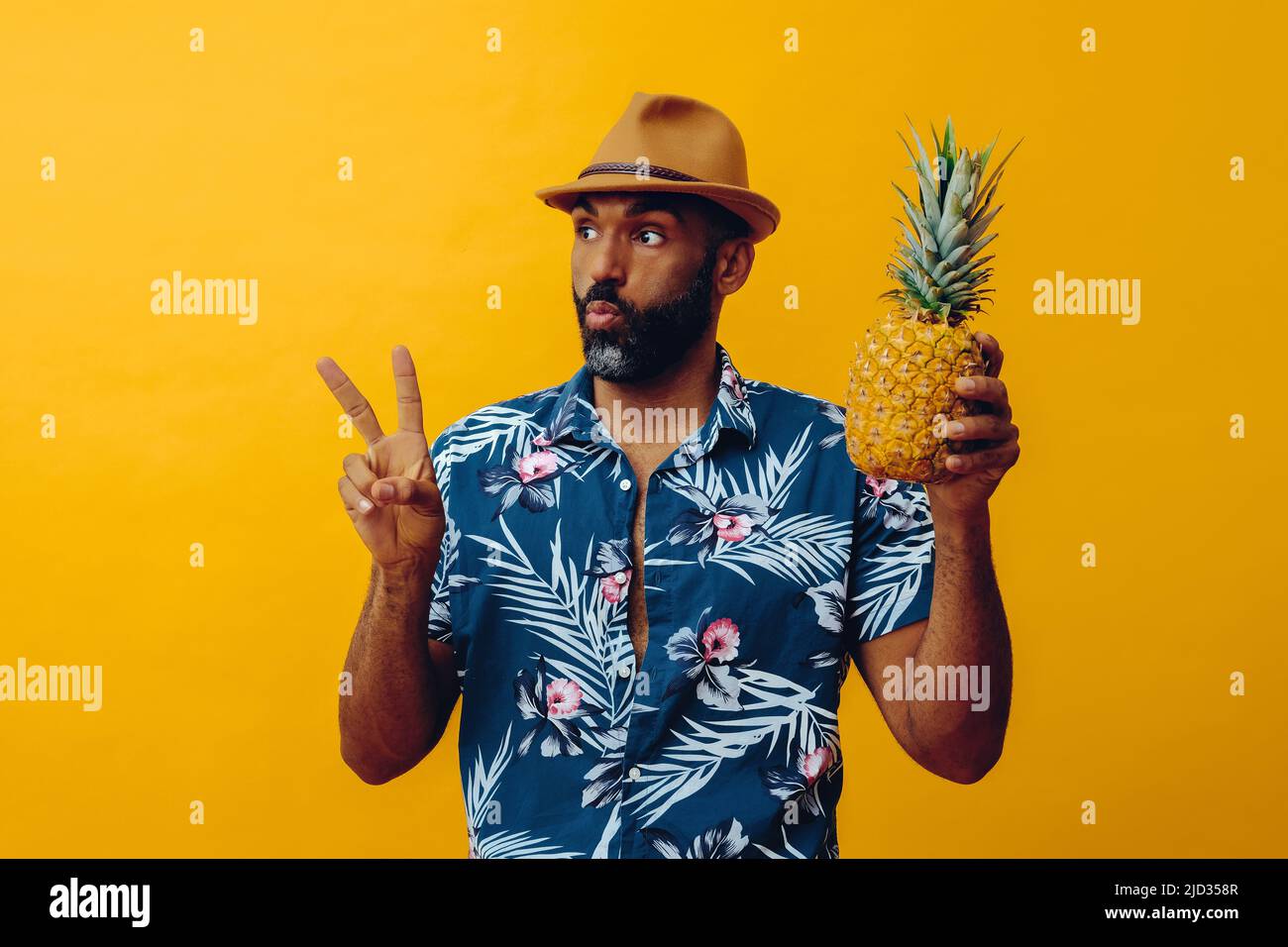 mid adult african american man in Hawaiian shirt posing with pineapple and peace sign fingers ...