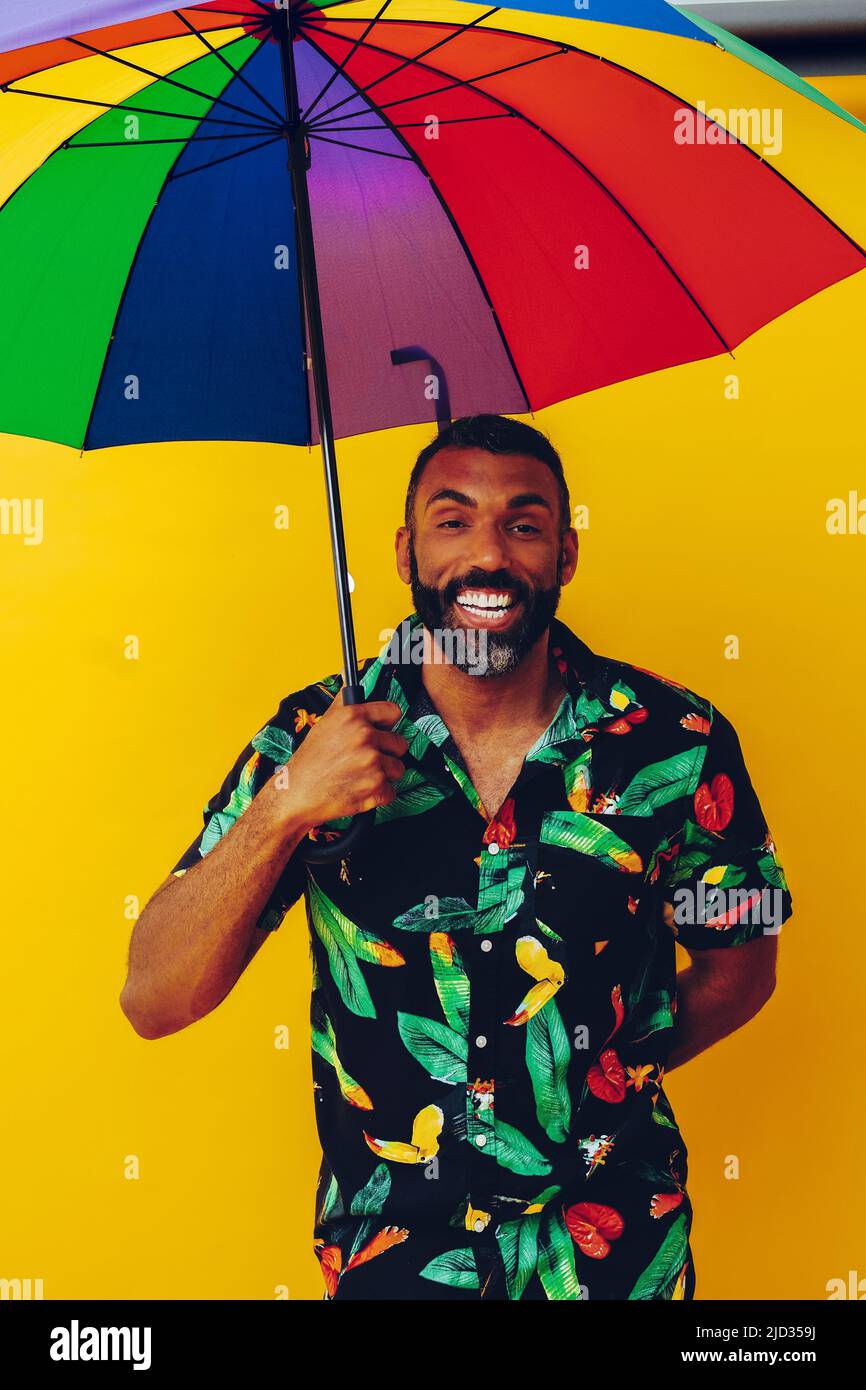 handsome smiling bearded african american man in Hawaiian shirt posing with colorful rainbow ...