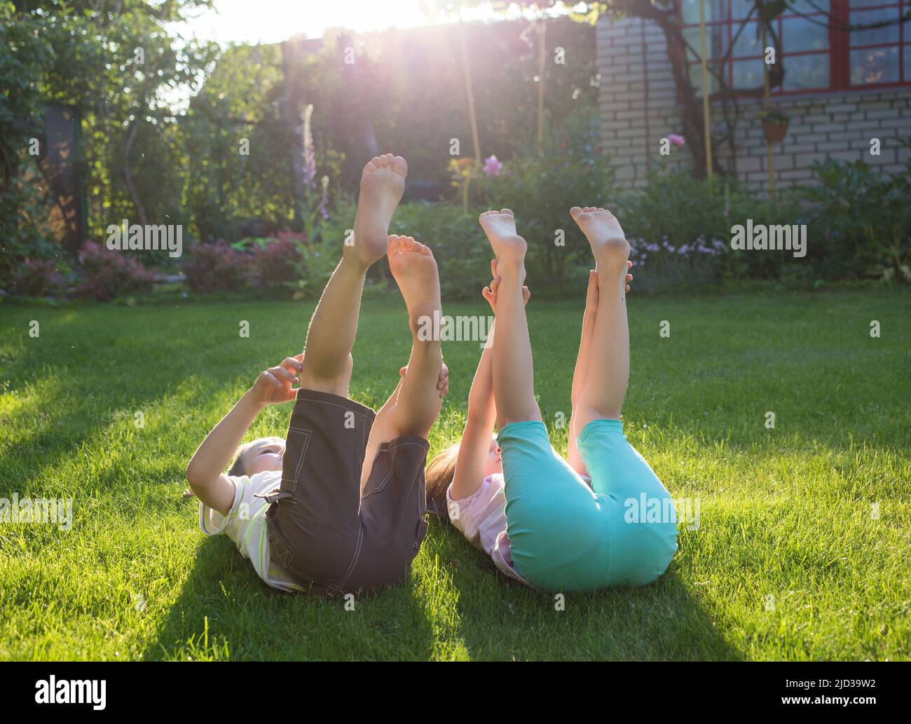 Two barefoot children lie on the grass with their feet up. cheerful ...