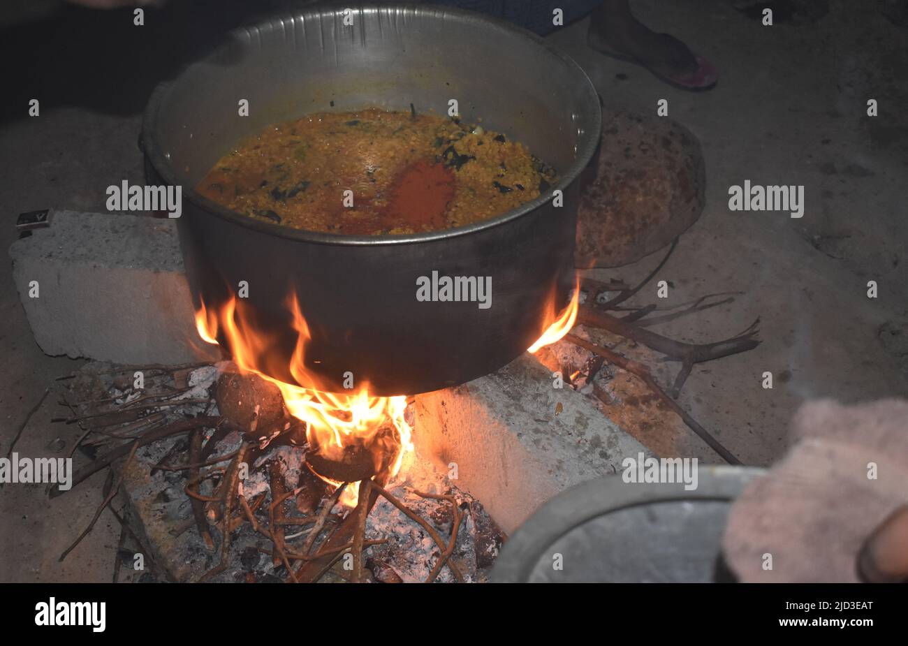 People cooking on a firewood stove. The stove is made out of 3 large ...
