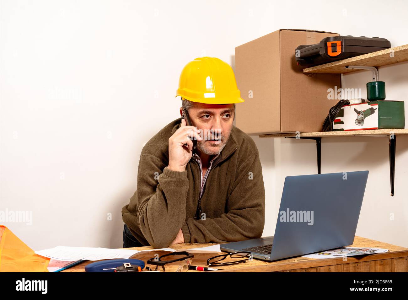 Contractor talking on cell phone with laptop in front of work office ...