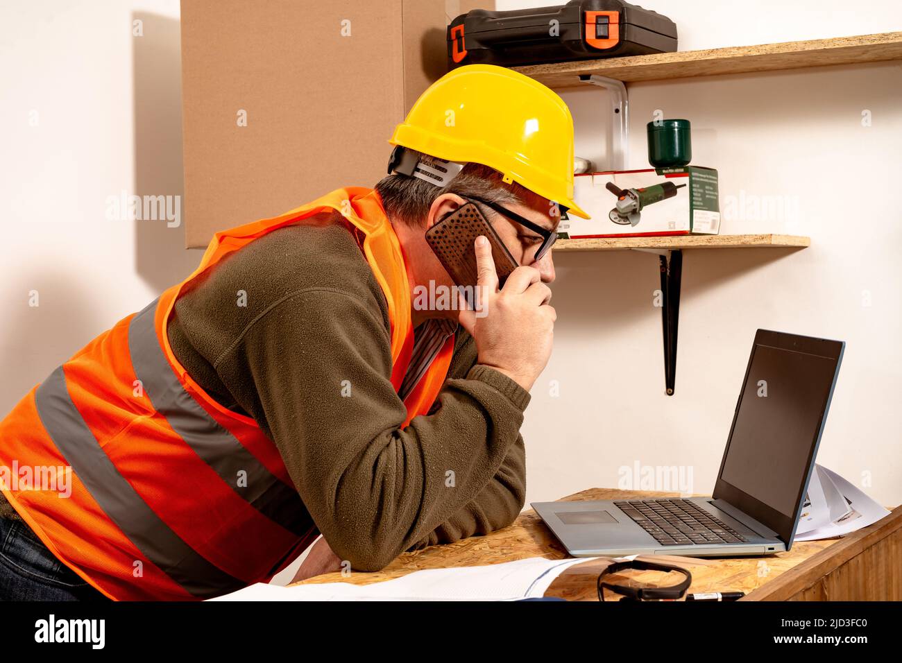 Contractor talking on cell phone while checking laptop in work office ...